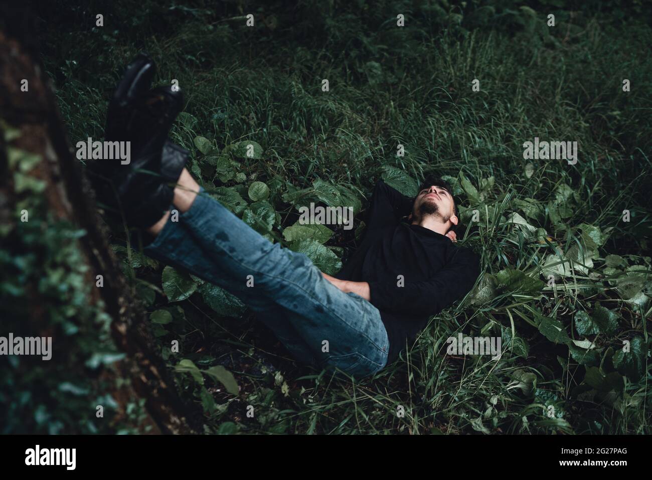 Handsome man in the forest stretches his feet to a tree and lies on the ...