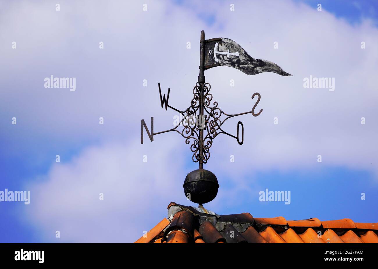 Old metal weather vane on the roof of a building with the four cardinal ...