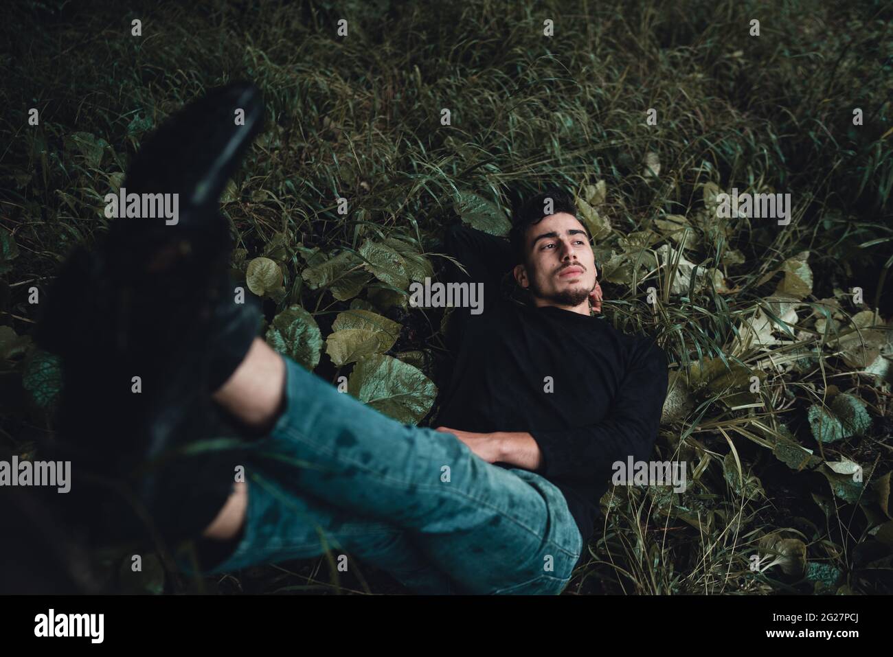 Handsome man in the forest stretches his feet to a tree and lies on the ...