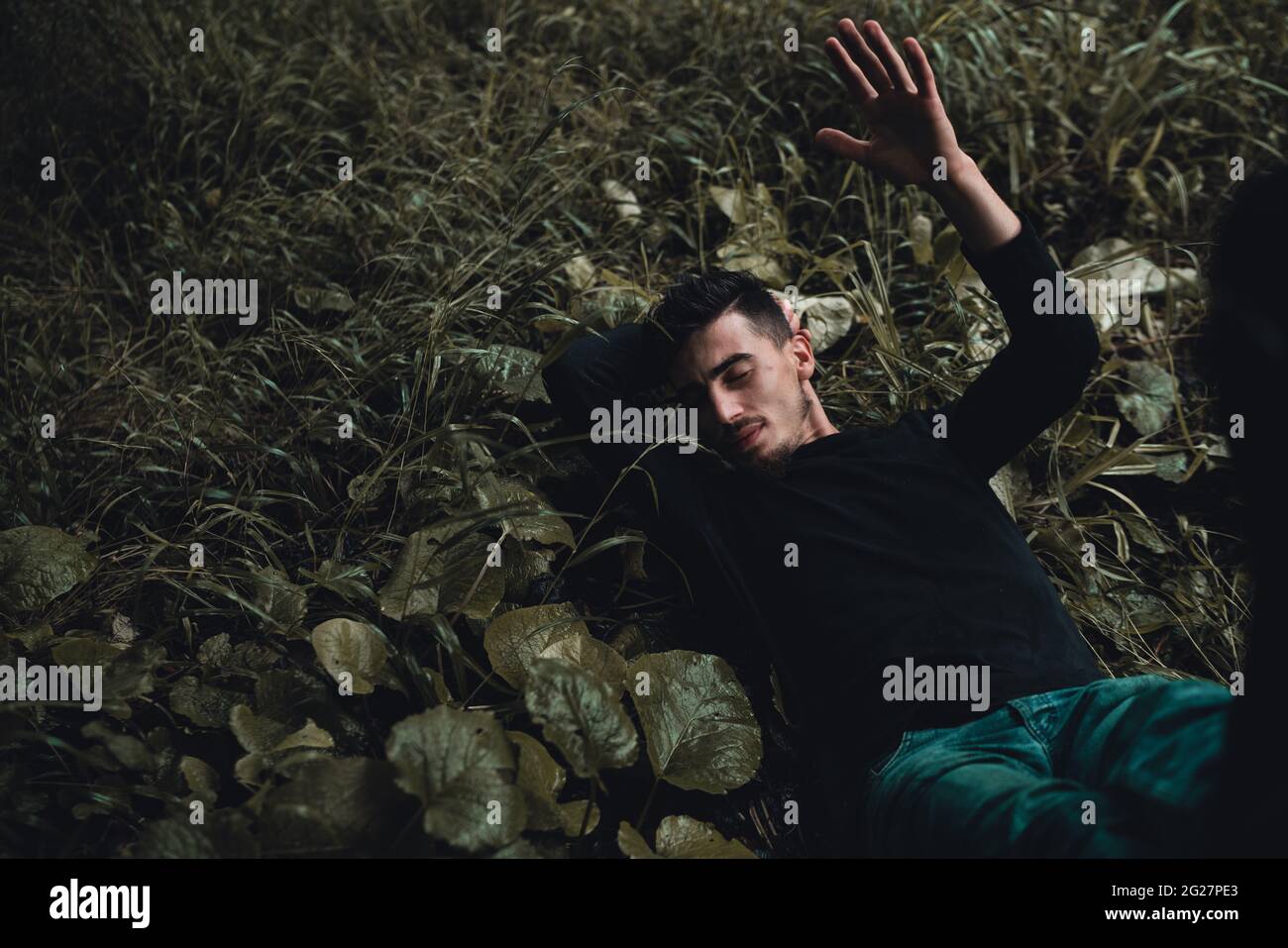 Handsome man in the forest stretches his feet to a tree and lies on the ...