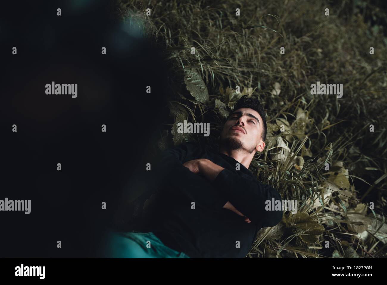 Handsome man in the forest stretches his feet to a tree and lies on the ...