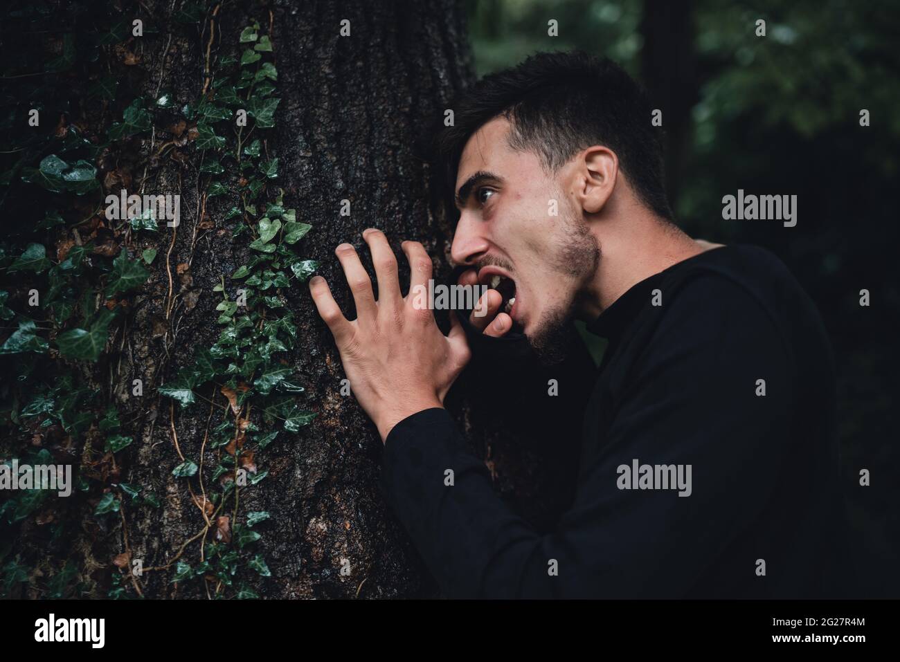A young man in the forest hugging the trees and screaming and ...