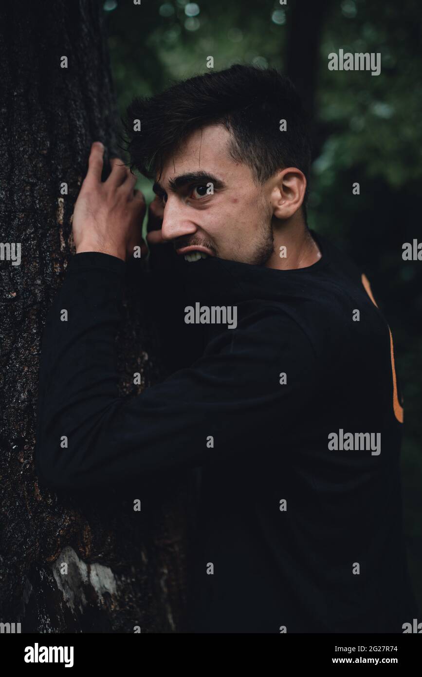 A young man in the forest hugging the trees and screaming and ...