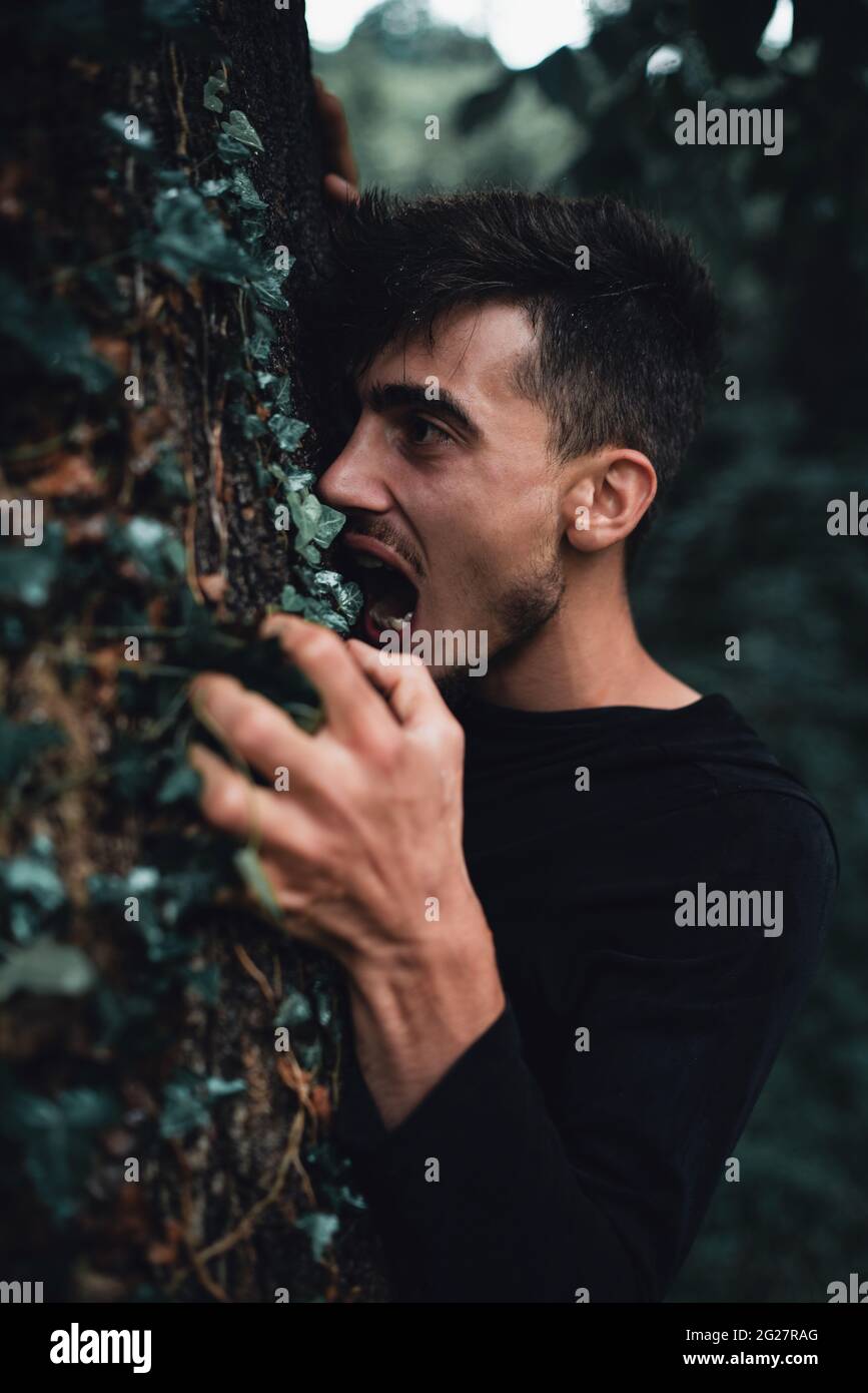 A young man in the forest hugging the trees and screaming and ...