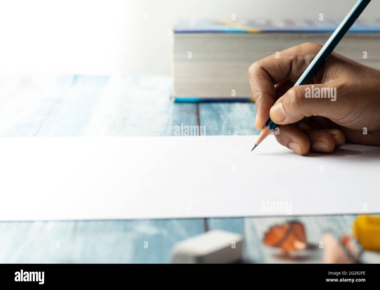 Close up view of hand and pencil writing on paper with books and white ...