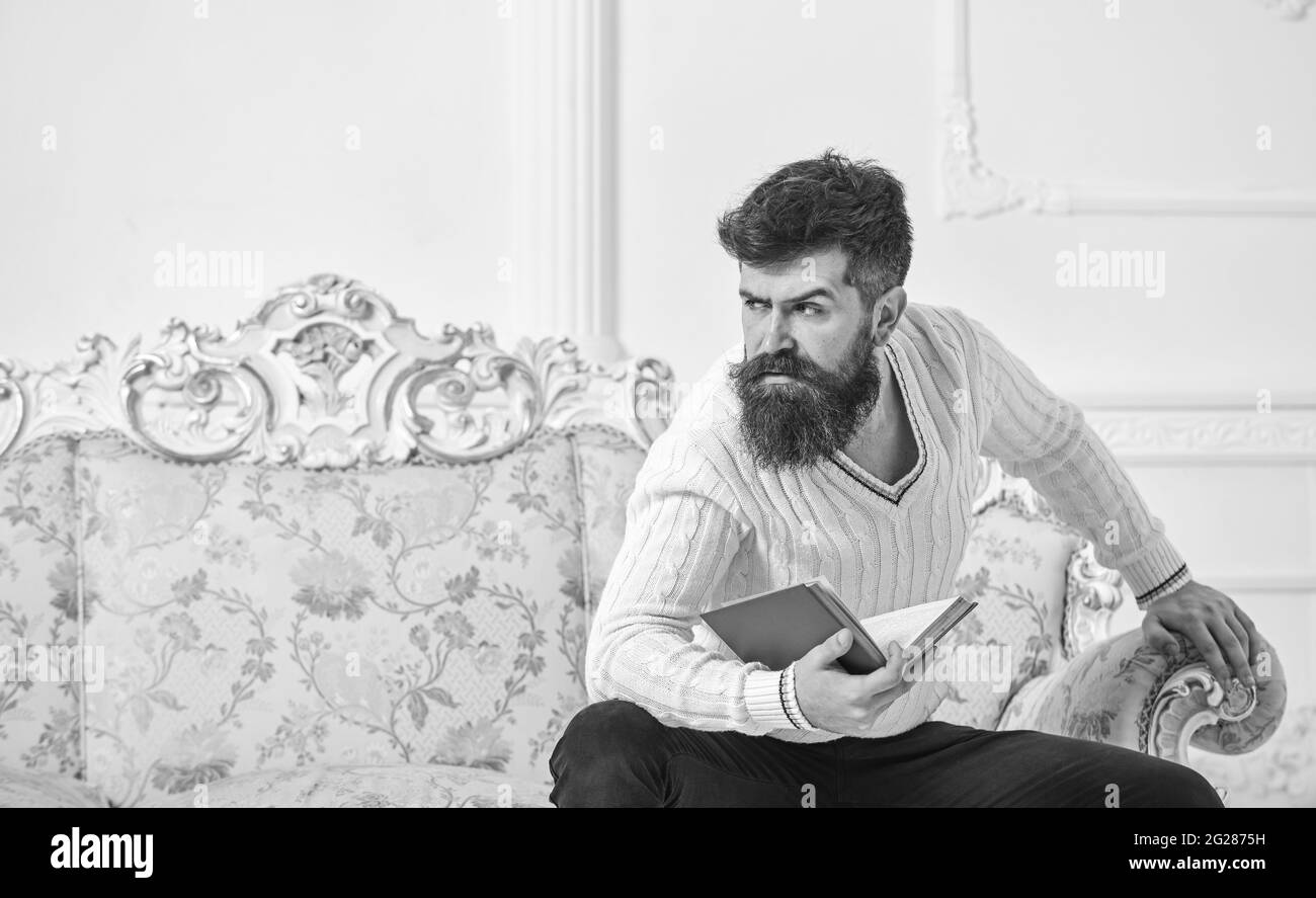 Man with beard and mustache sits on baroque style sofa, holds book ...