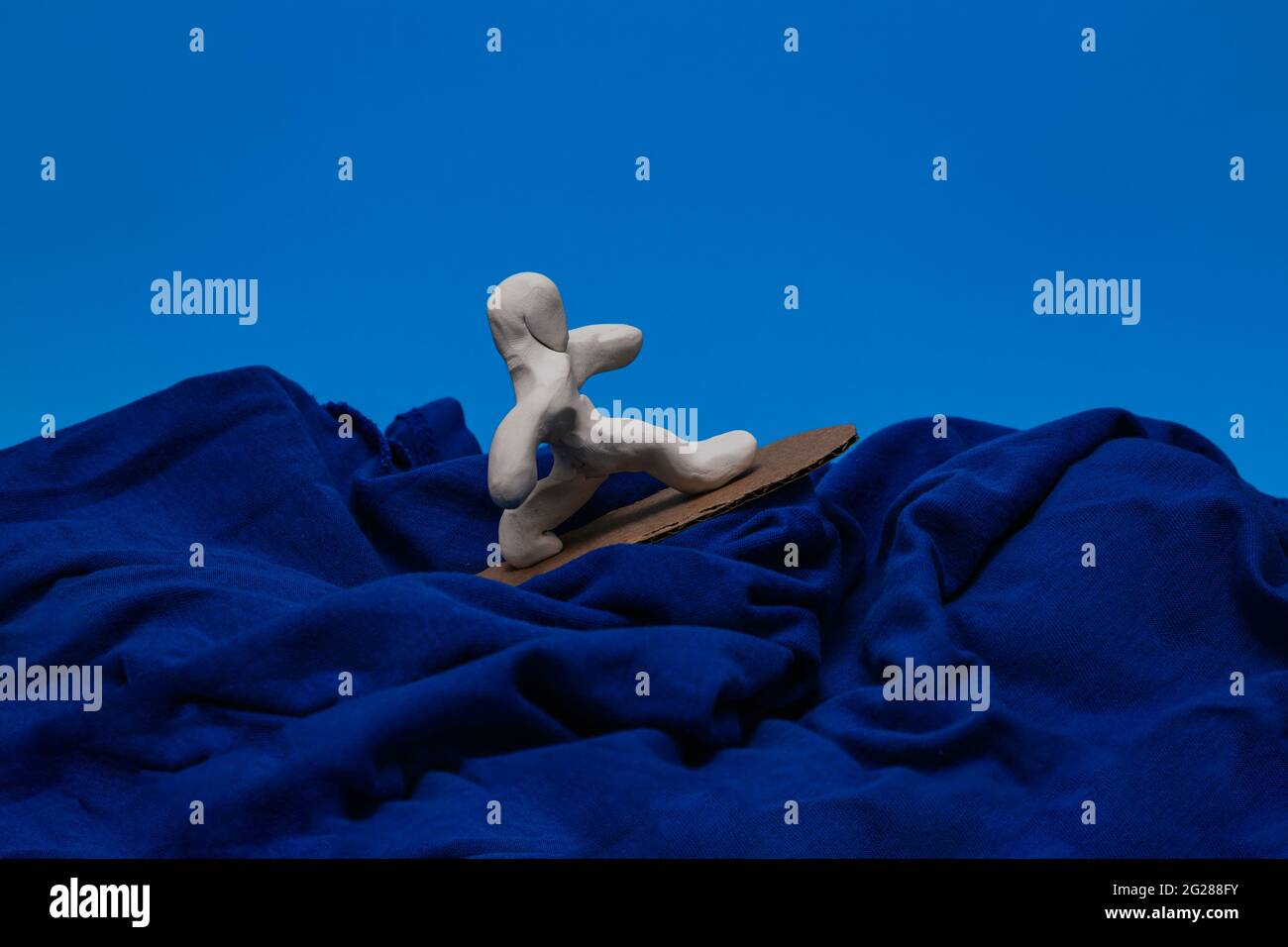 A white plasticine doll surfing on a blue background. The doll is ...