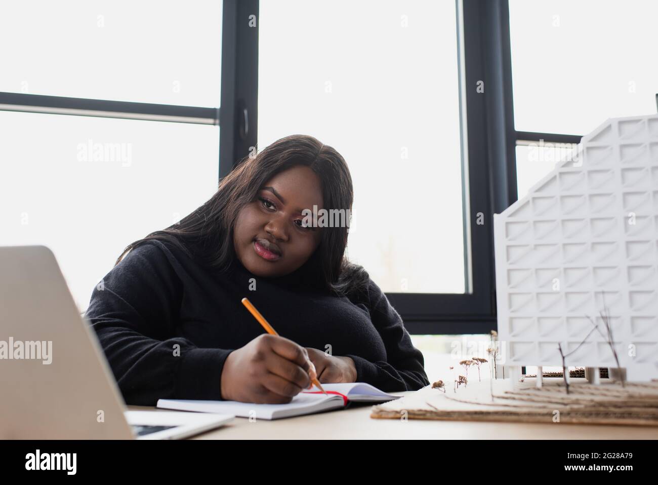 african american plus size designer writing in notebook while looking ...