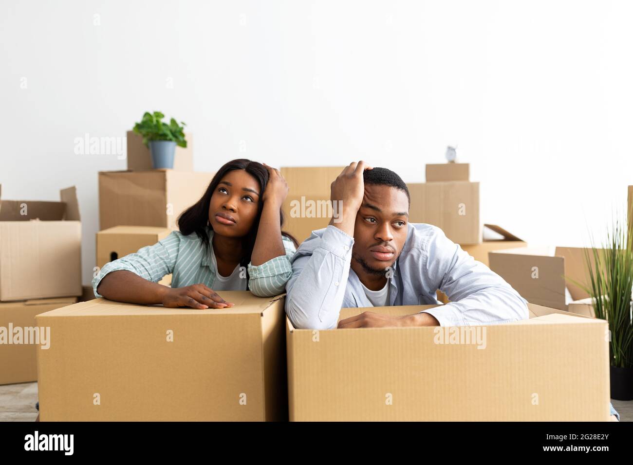 Sad and tired black couple leaning on unpacked boxes, sitting in the ...