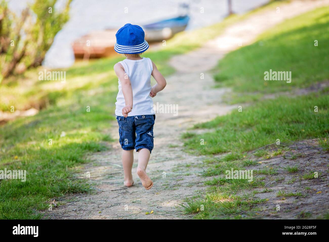 Sweet toddlel child, running on a path next to a lake with boats ...