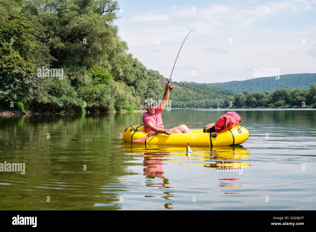 Mature man fishing from the packraft yellow boat on the river at summer ...