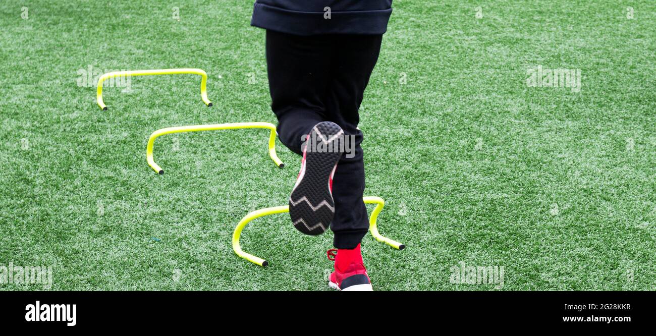 A high school track athlete is jumping over six inch yellow mini ...