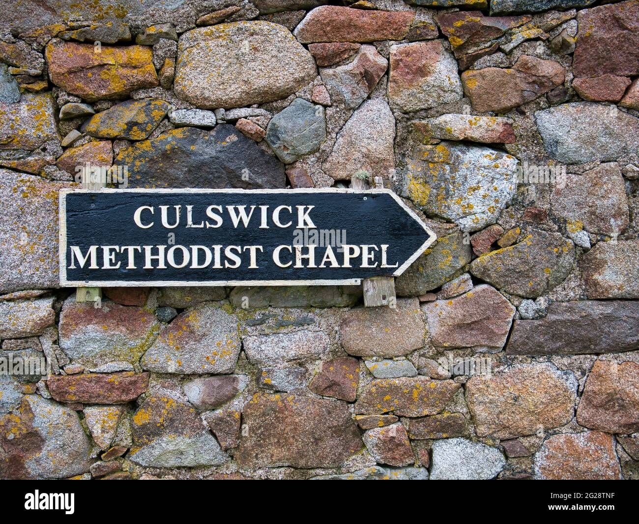 A wooden sign on a colourful, old stone wall points the way to the ...