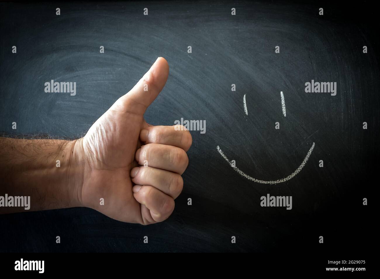 Thumb up beside a smiley face drawn in chalk on a blackboard, concept ...