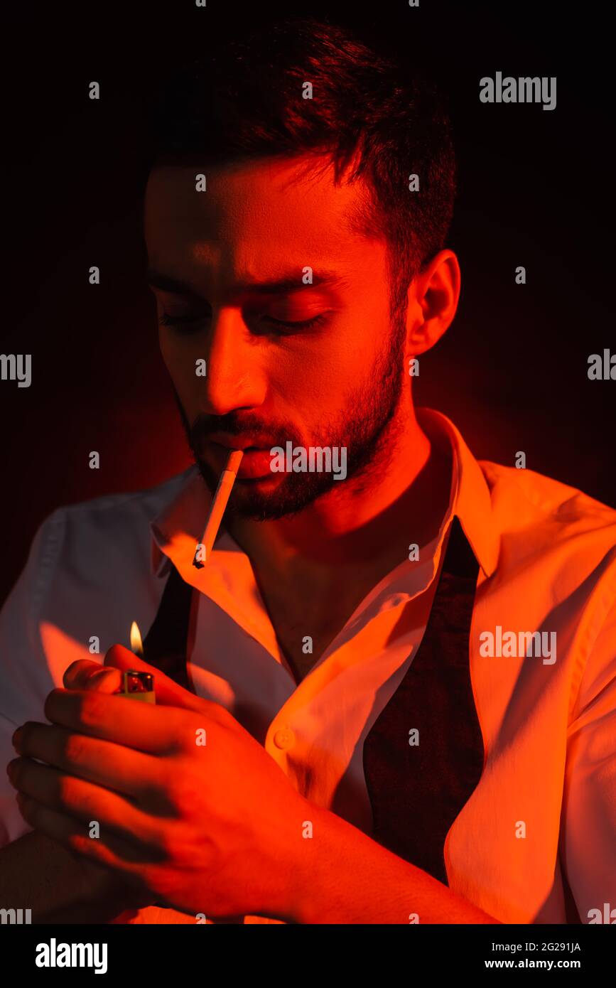 Bearded man with cigarette holding lighter in red light on black ...