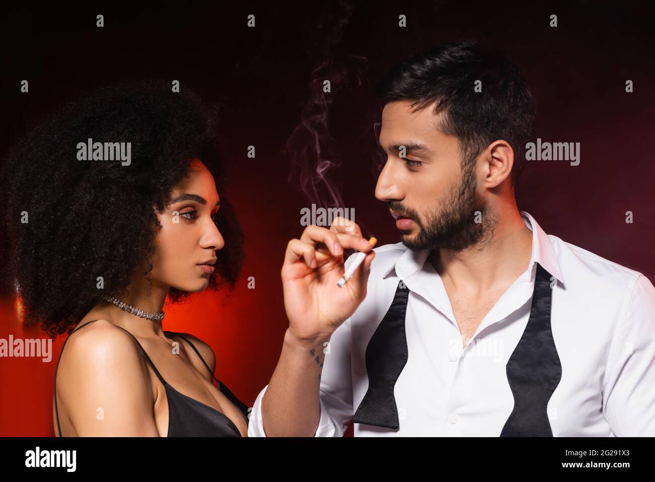 Man smoking cigarette near elegant african american girlfriend on black ...