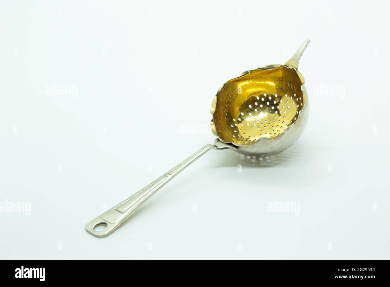 A shiny old tea sifter with gold plated base and long holder Stock ...