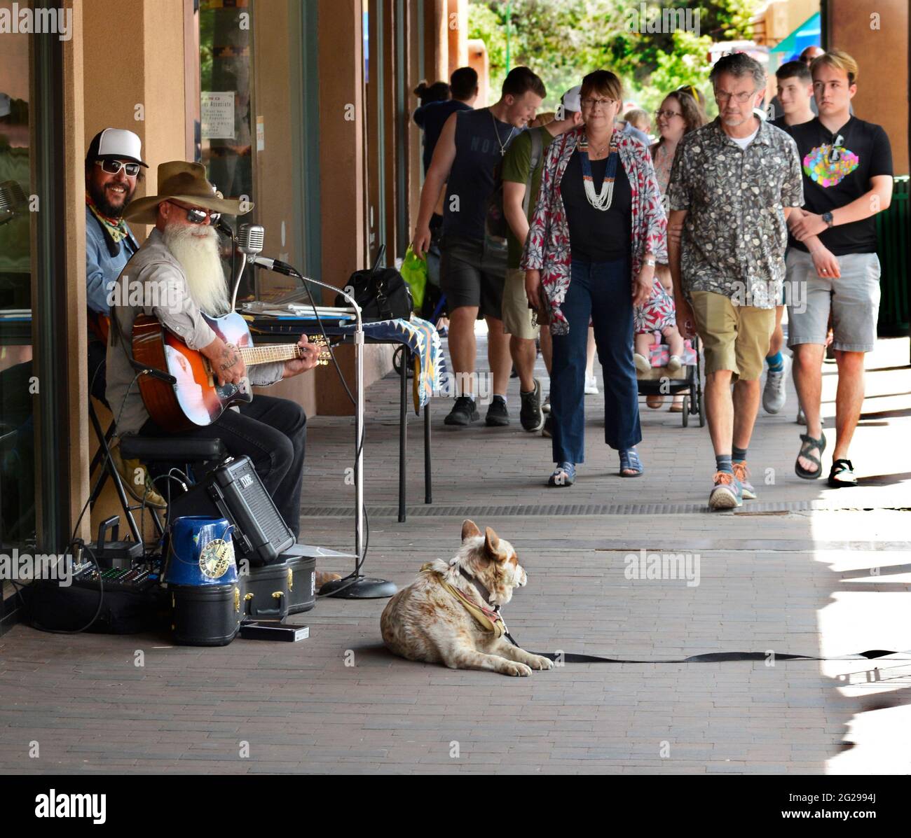 A busker sings and plays his guitar for tips on a sidewalk in front of ...