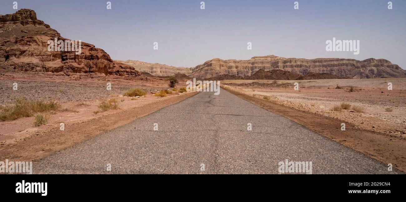 A narrow road leading to distant mountains, in the Timna valley desert ...