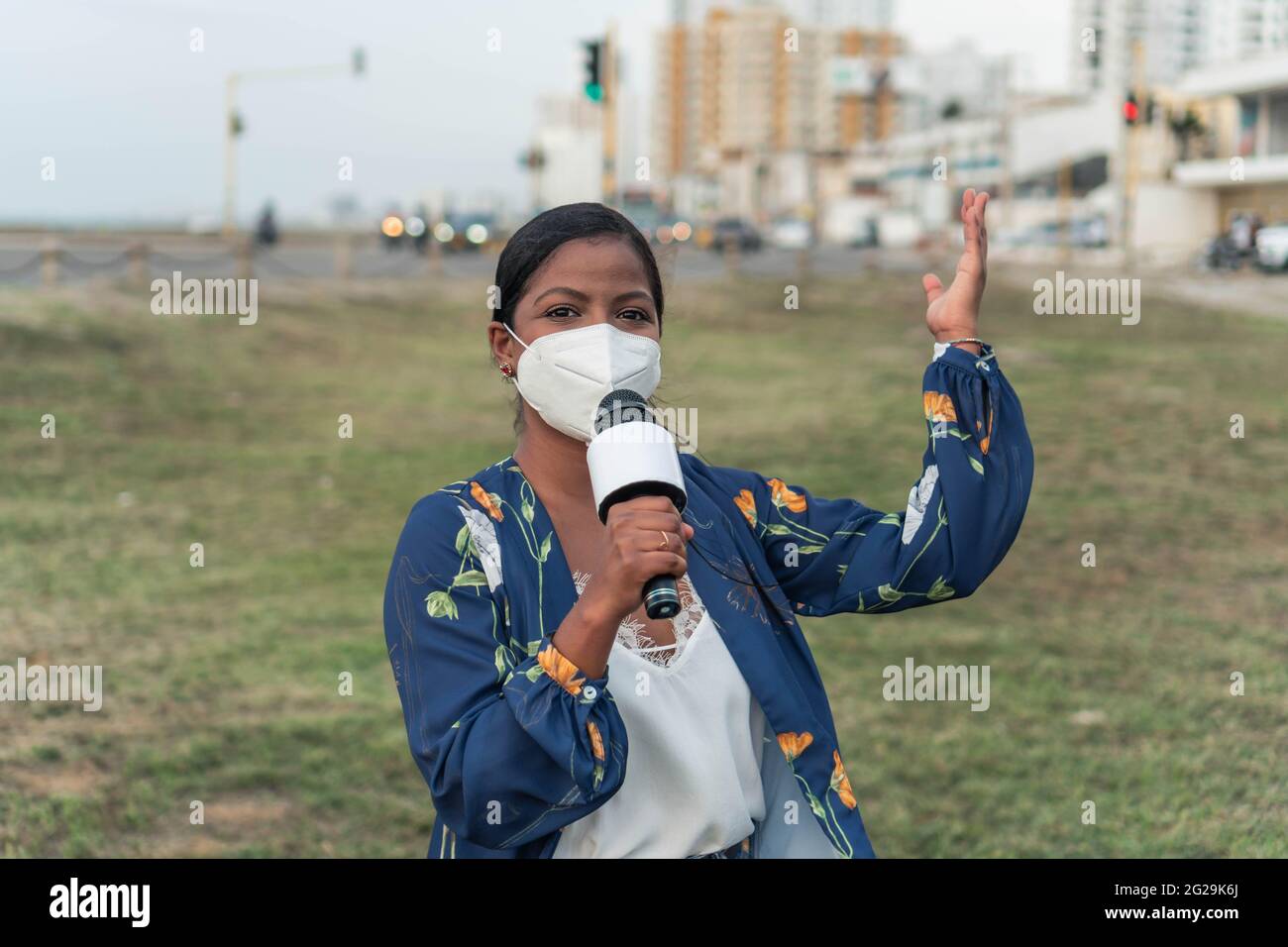 Black woman reporter in mask speaking into microphone on the street in ...