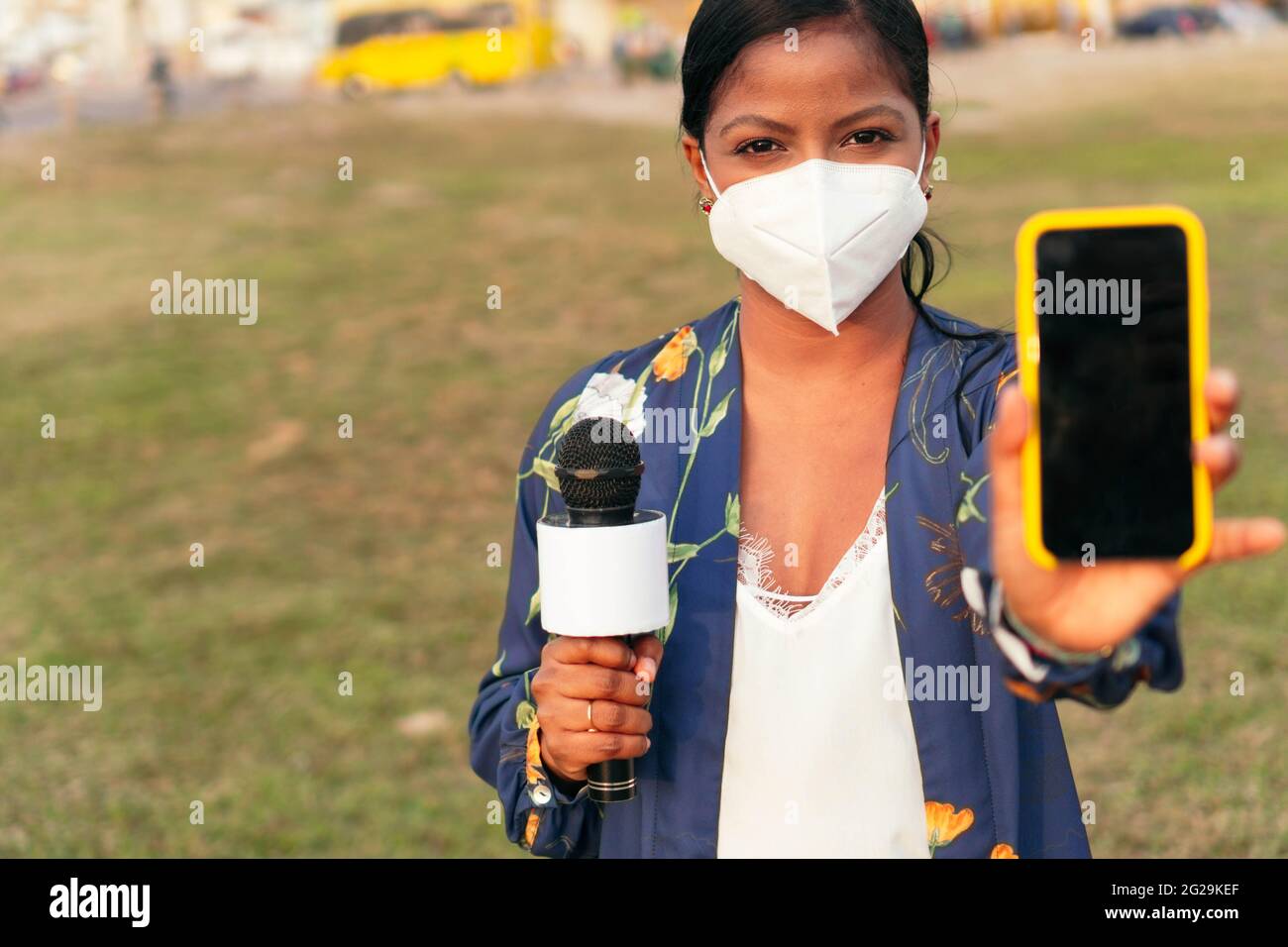 Female journalist wearing mask showing smart phone while standing in ...