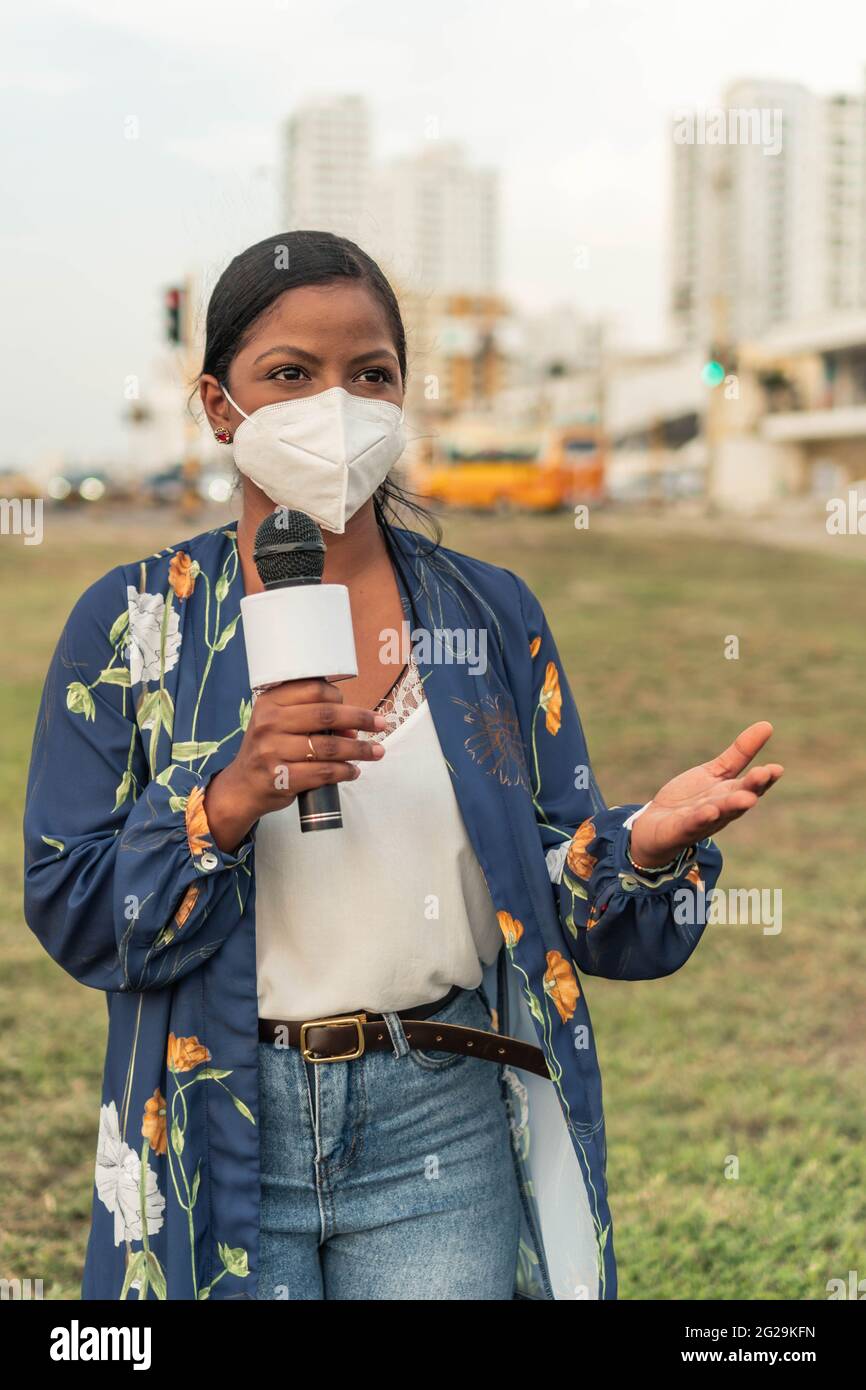 African woman reporter in mask speaking into microphone while standing ...