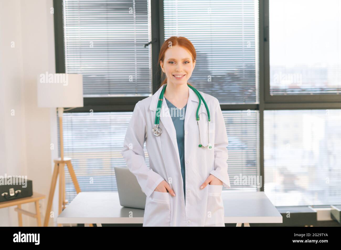 Portrait of smiling female doctor in white coat standing on background ...