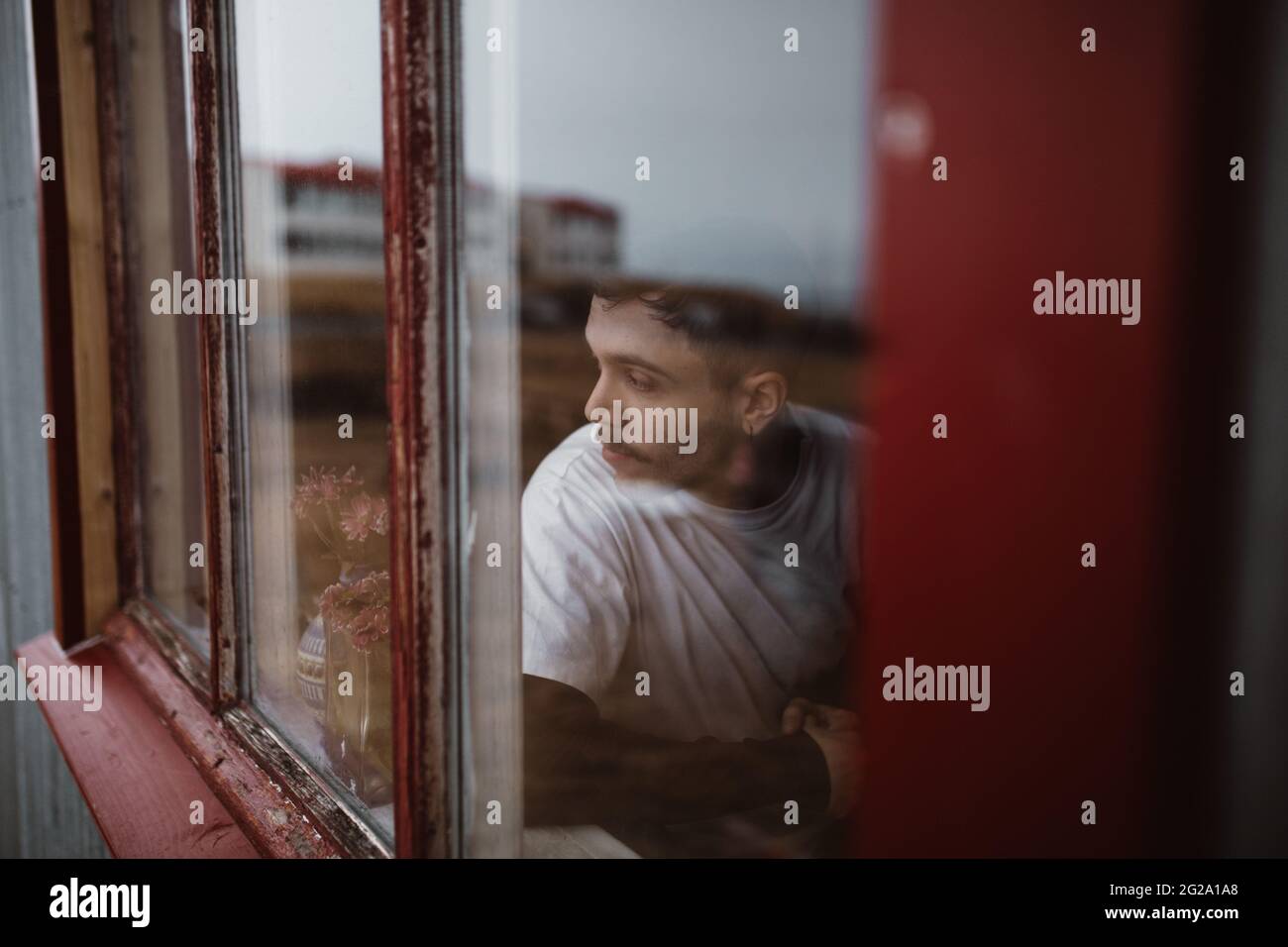 Shot through glass of young man sitting behind window of old house ...