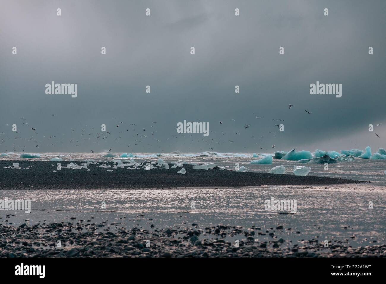 Black empty coast of ocean with rough cliffs in snow under heavy grey ...