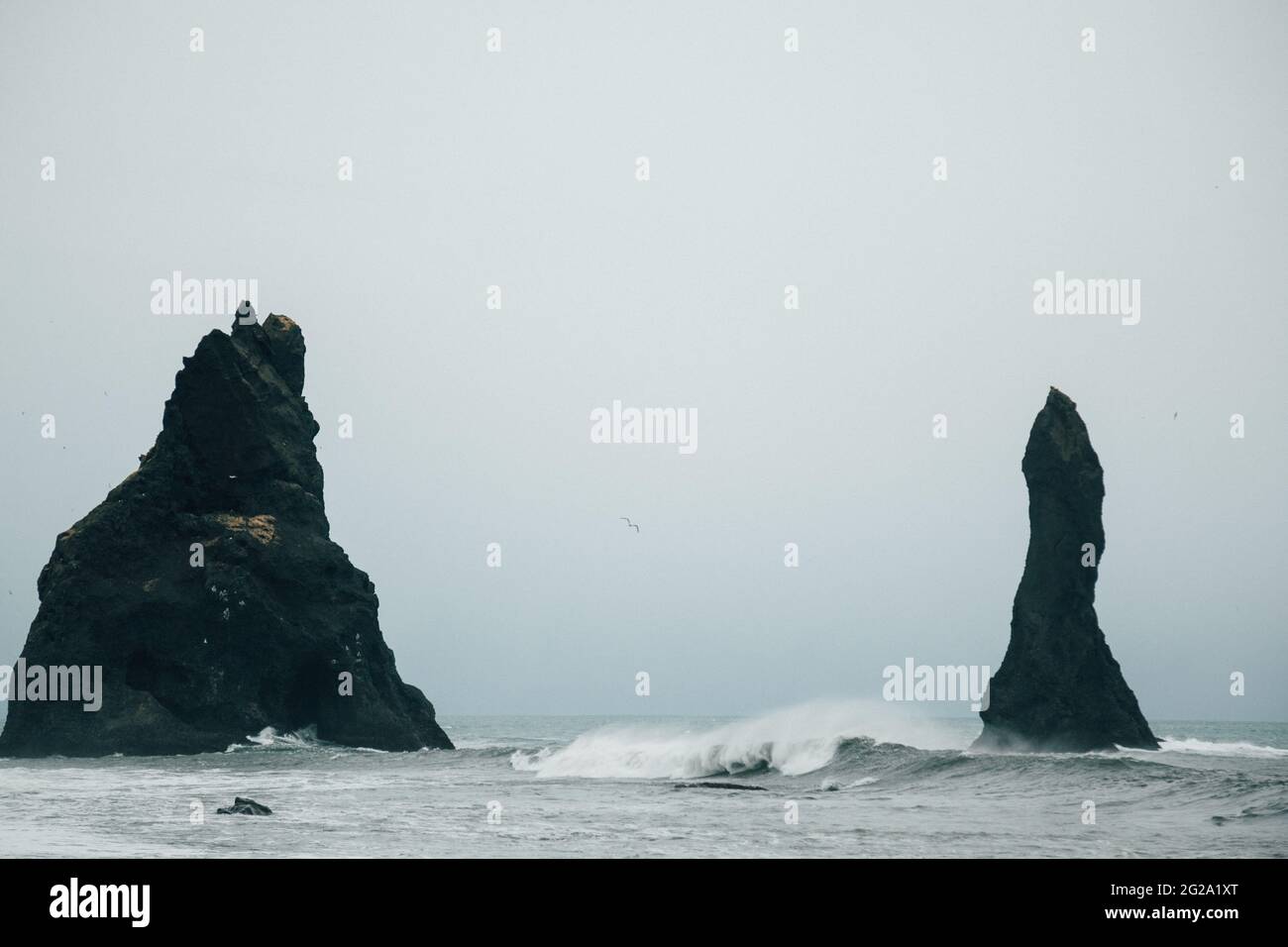 Huge black sharp peak of cliff in ocean water with waves running on ...