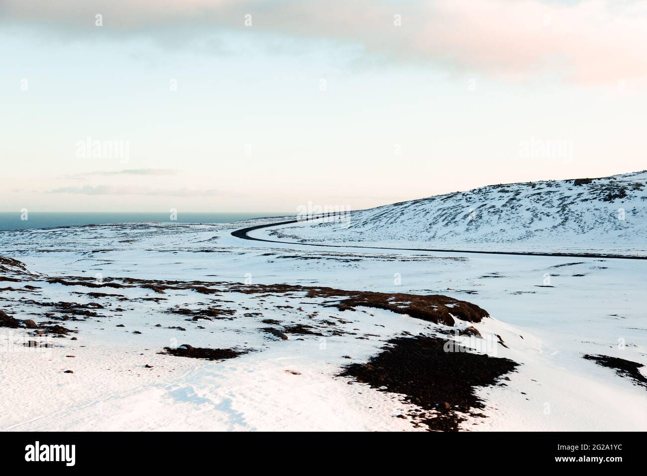 Curvy asphalt road going through white snowy terrain against gray sky ...