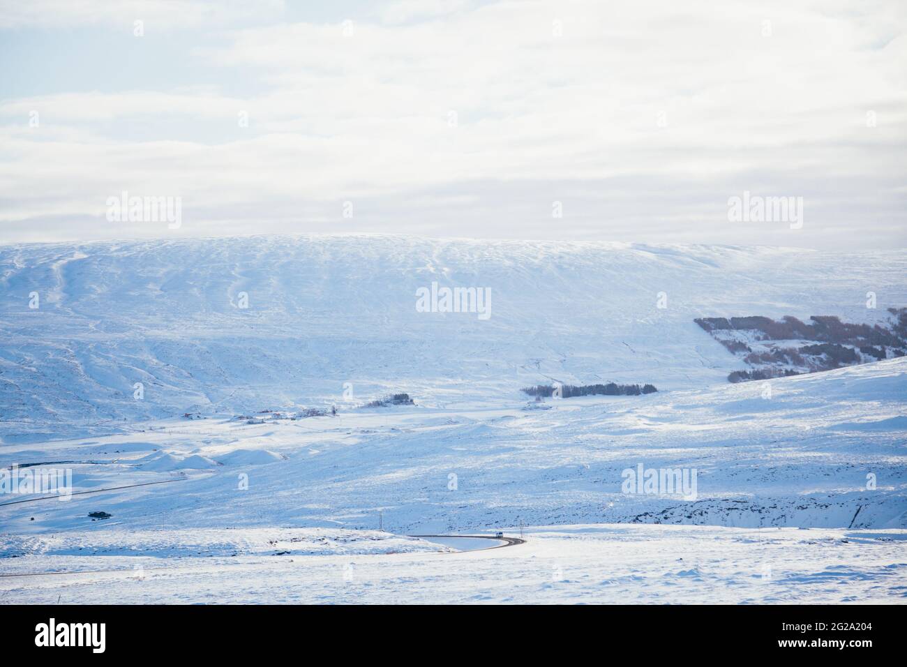 Curvy asphalt road going through white snowy terrain against gray sky ...
