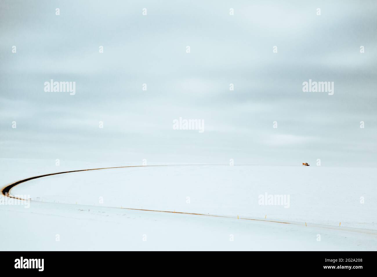 Curvy asphalt road going through white snowy terrain against gray sky ...