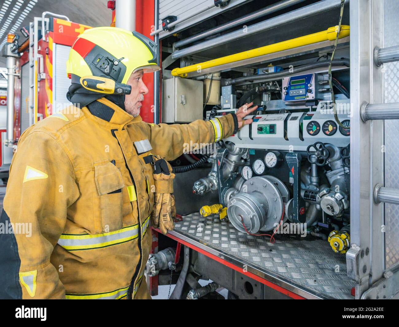 Equipped fireman standing and using an water engine into fire truck ...