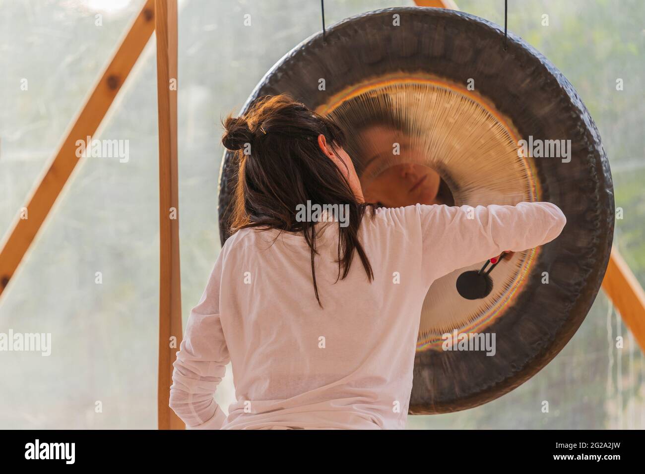 Back view of balanced Woman in white clothes hitting gong while ...
