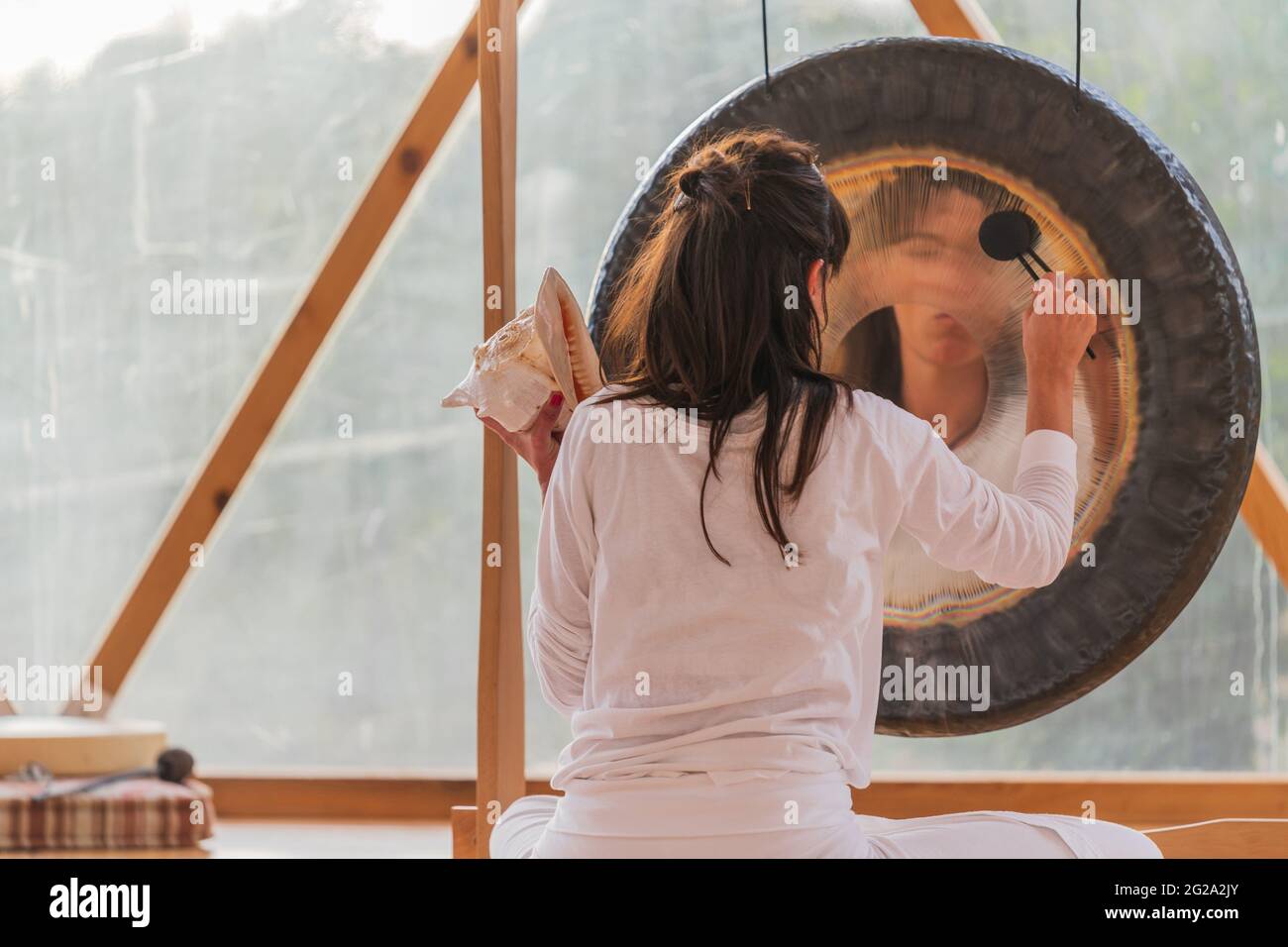 Back view of balanced Woman in white clothes hitting gong while ...