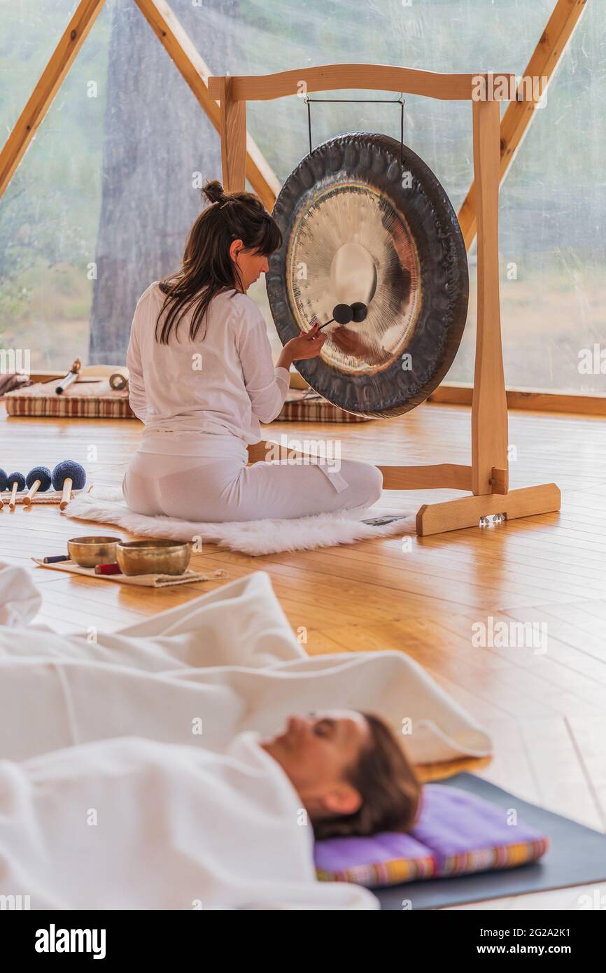 Back view of balanced Woman in white clothes hitting gong while ...