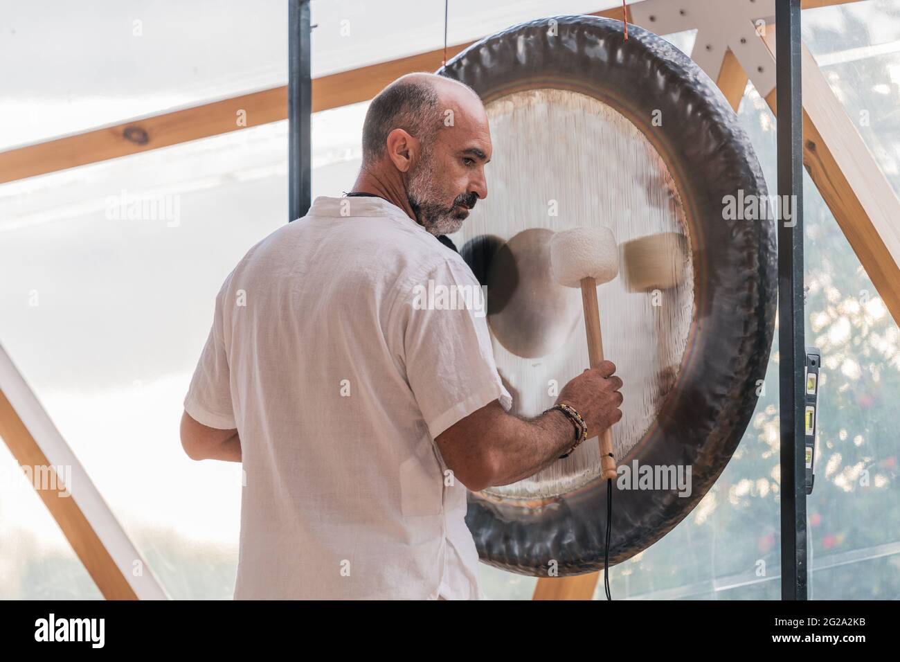 Side view of balanced man in white clothes hitting gong Stock Photo - Alamy