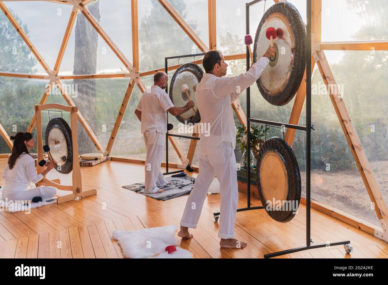 Side view of men and Woman in white clothes hitting gong in light room ...