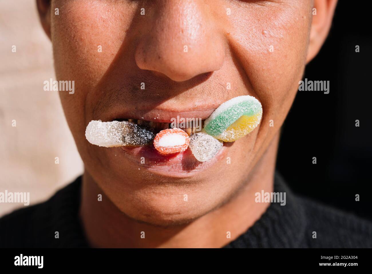 Crop ethnic person holding small sweet candy in decayed teeth on sunny ...