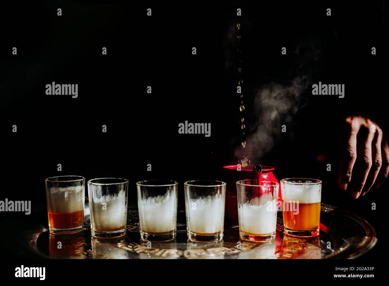 Steamy teapot and glass cups with hot tea placed on tray against black ...