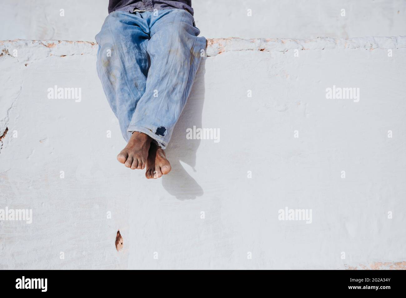 Barefoot legs of anonymous African kid in jeans sitting on shabby white ...