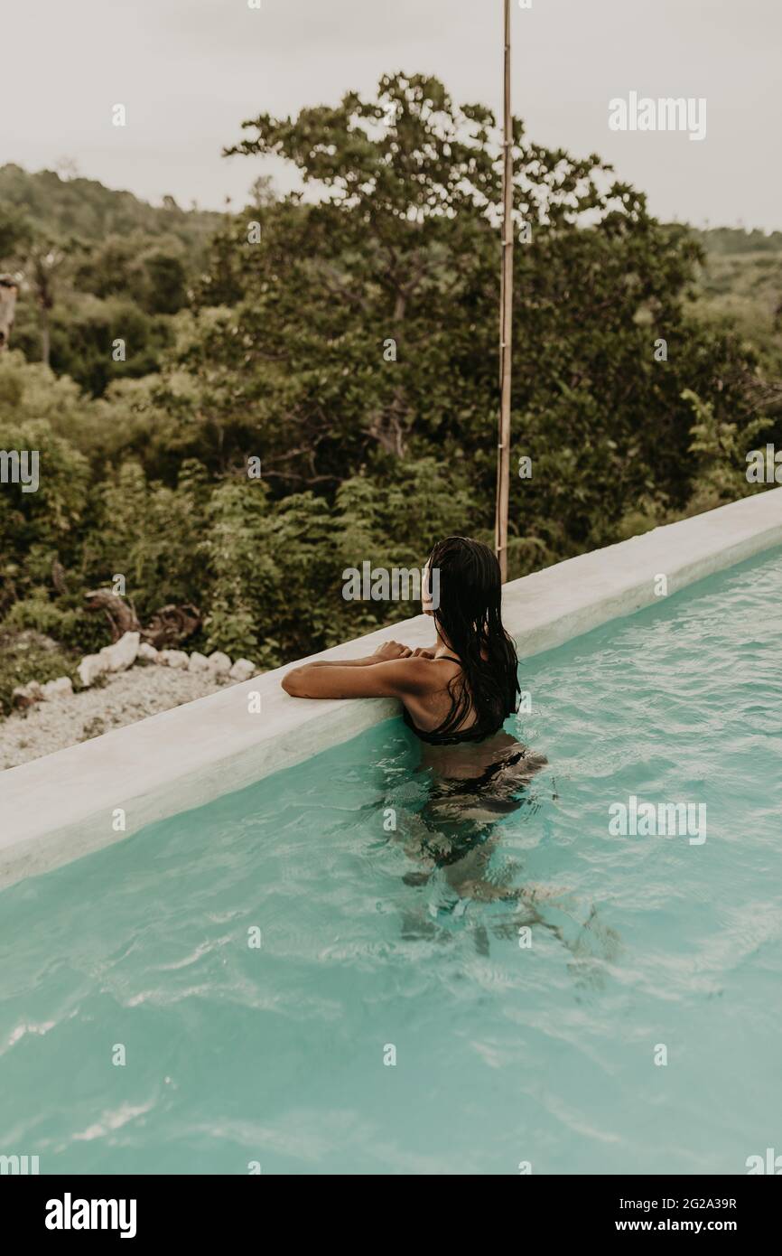 Back view of female swimming in pool against beautiful jungle landscape ...