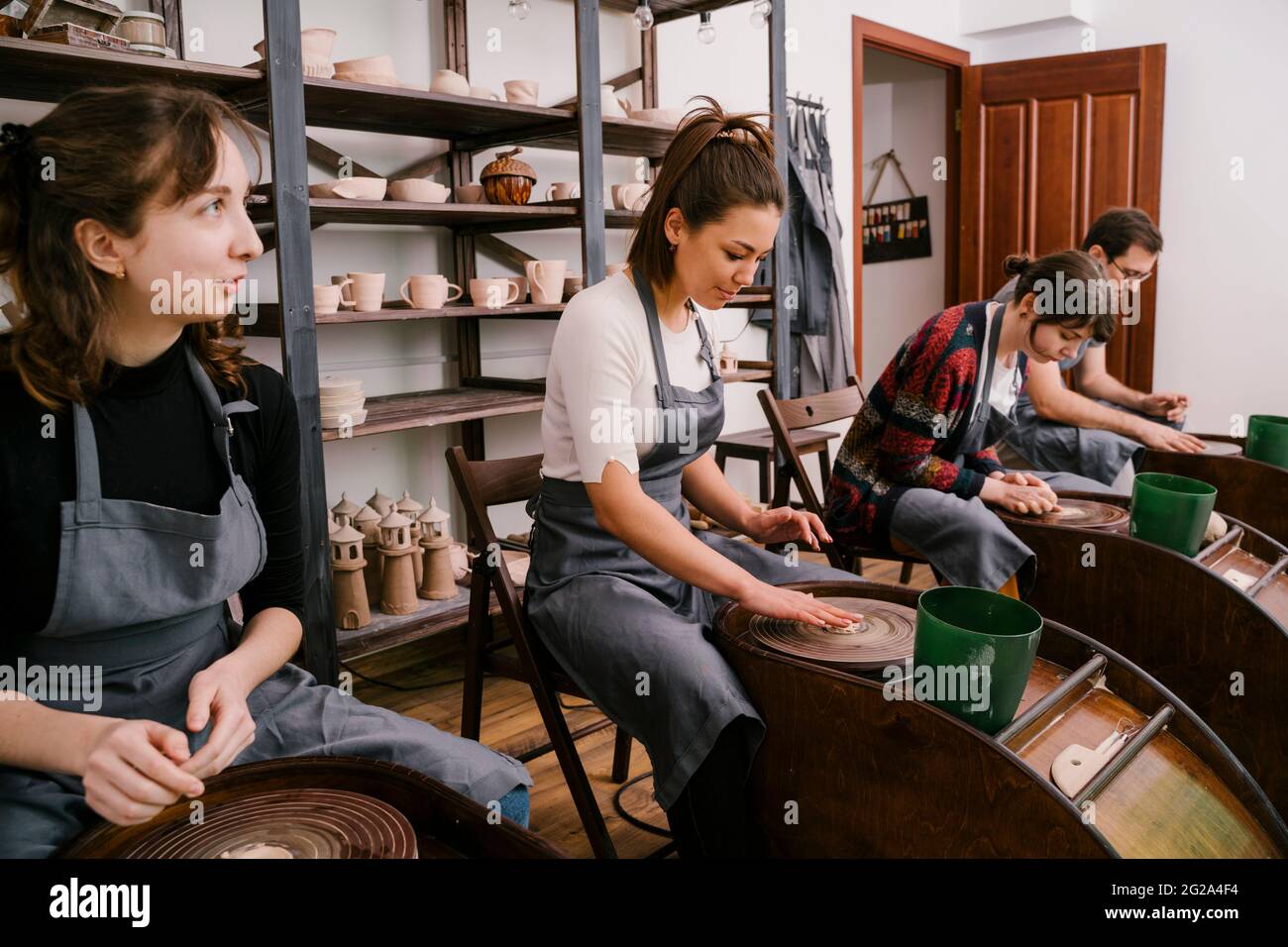 Enthusiastic people in aprons working with clay sculpting on pottery ...