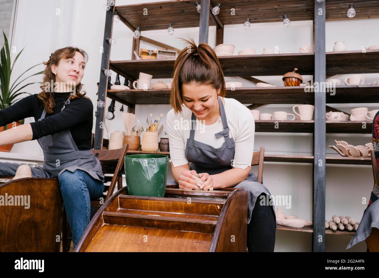 Women in apron behind pottery wheel working with clay material trying ...