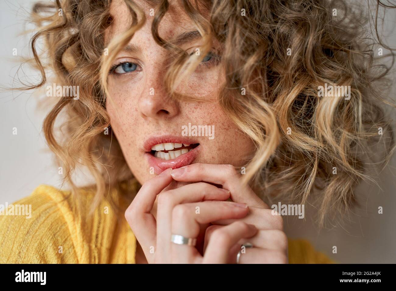 Charming blonde curly Woman touching face and thoughtfully looking at ...