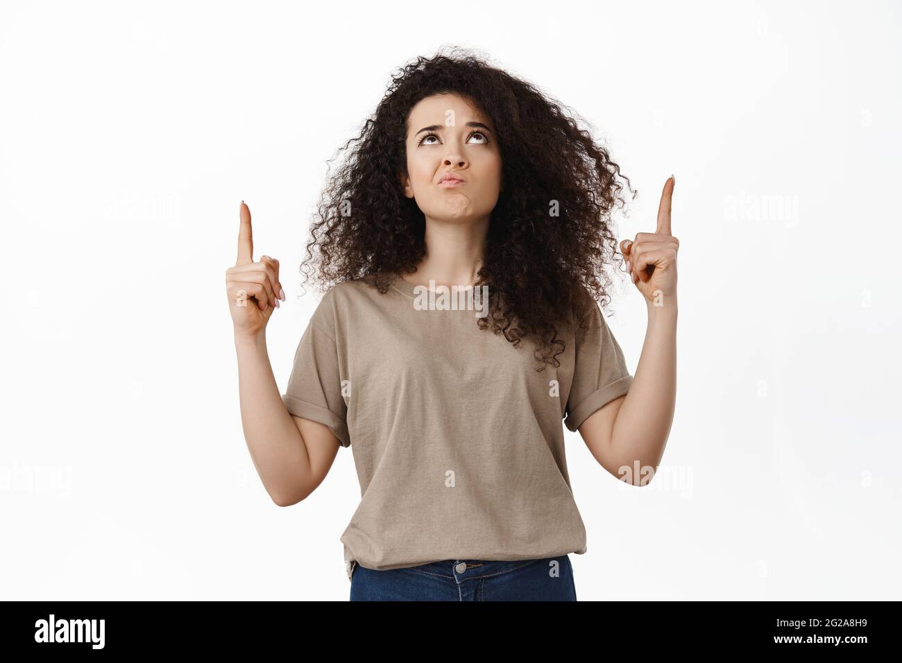 Indecisive and unsure brunette woman pointing fingers up and look ...