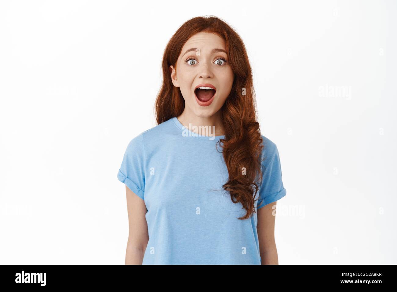 Surprised and impressed redhead woman drop jaw, stare amazed at camera ...
