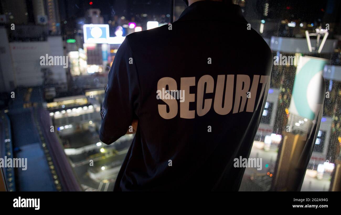 Back view of a security guard looking down the city full of lights at ...