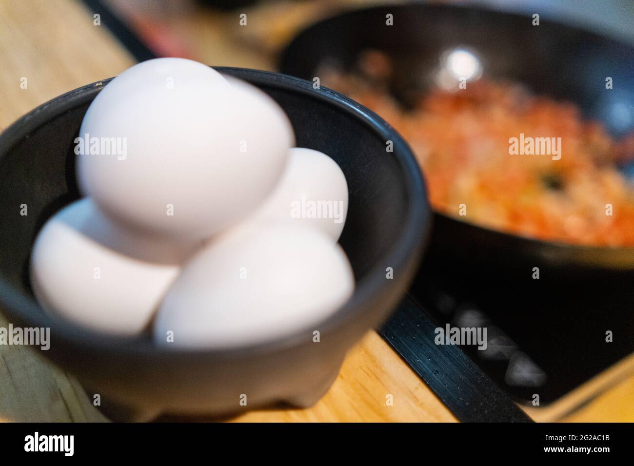 Eggs in small black bowl with blurry food in pan as background Stock ...